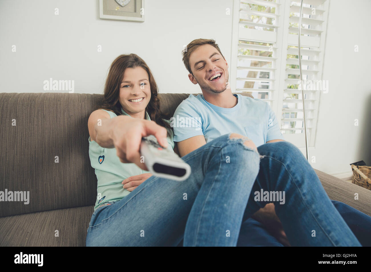 Couple on sofa using remote control smiling Stock Photo - Alamy