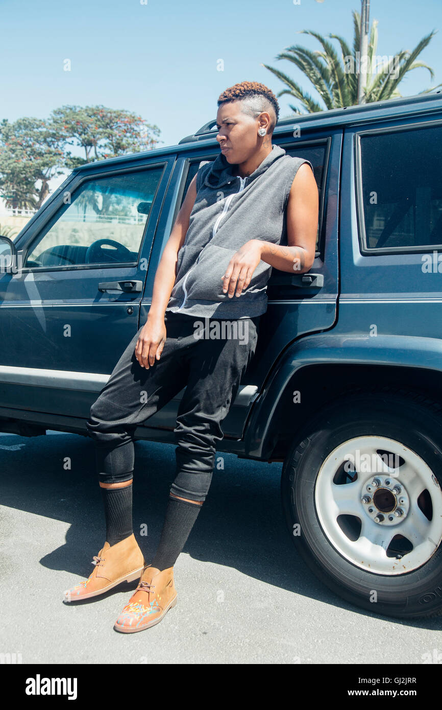 Woman leaning against car looking away Stock Photo - Alamy