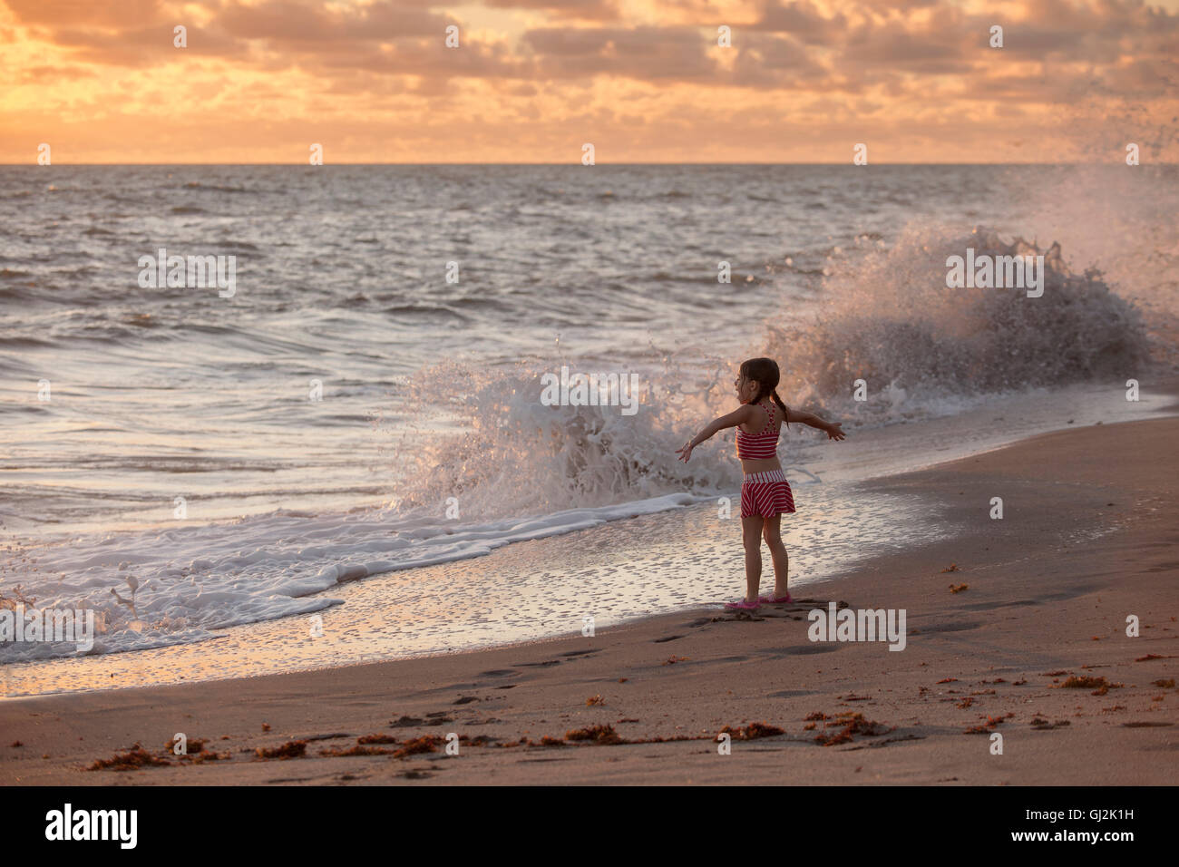Girl with arms open whilst waves splash at sunrise, Blowing Rocks ...