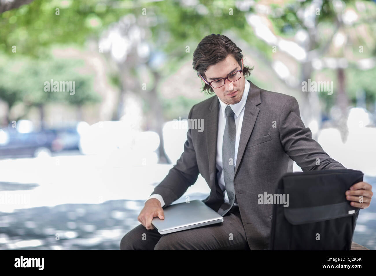 Businessman sitting in park removing laptop from briefcase Stock Photo ...