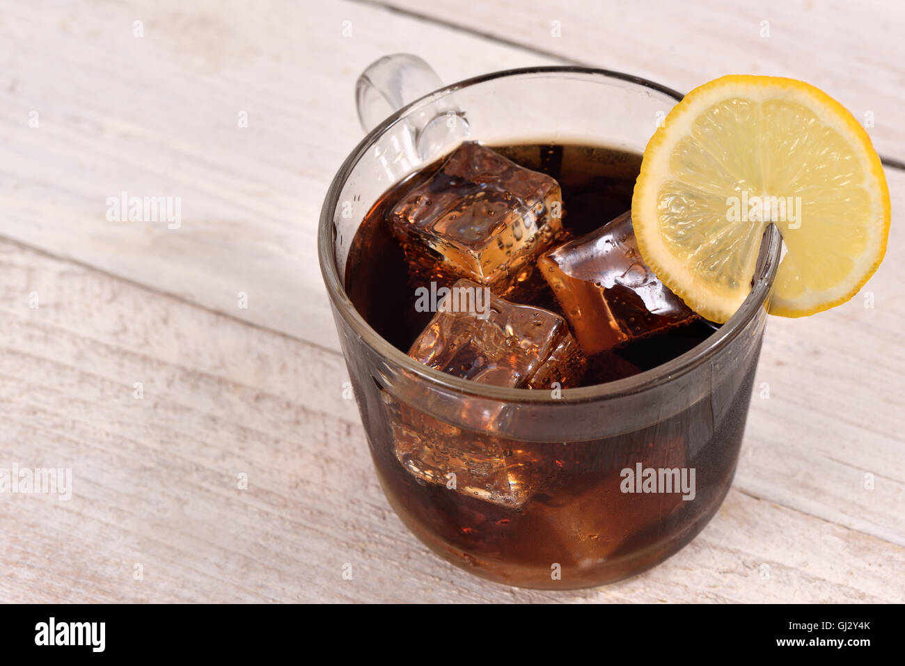 Cola drink with ice cube and lemon slice on white rustic wood ...