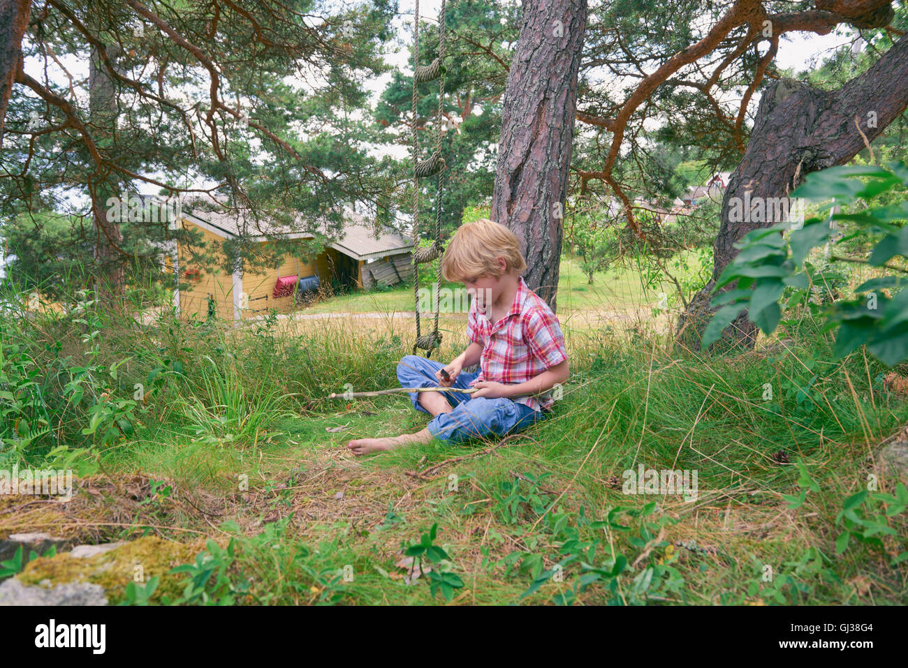 Young boy sitting outdoors, cleaning tree branch with knife Stock Photo ...