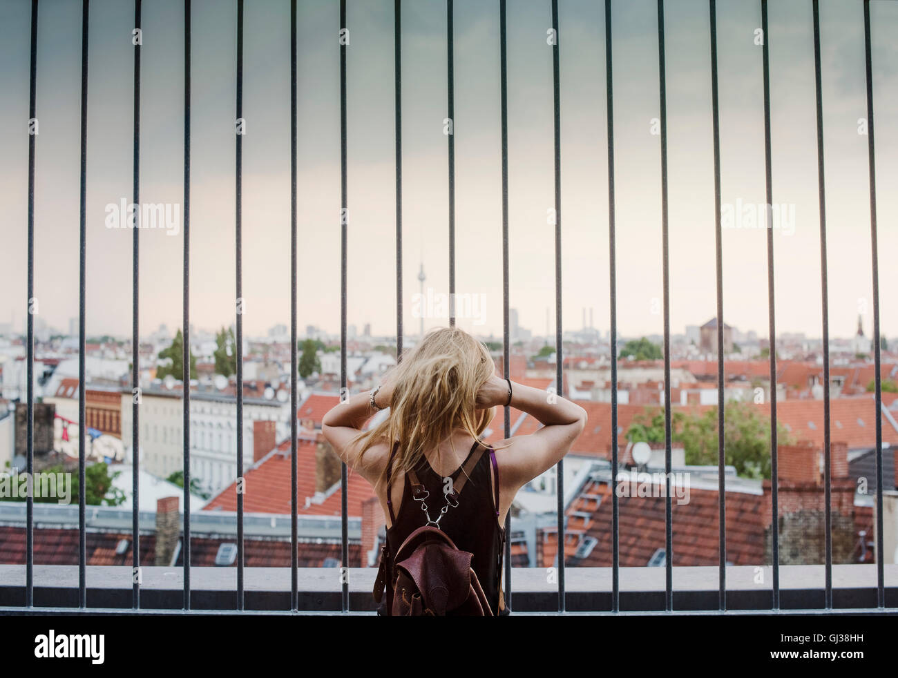 Young woman looking through railings, at view across rooftops, rear ...