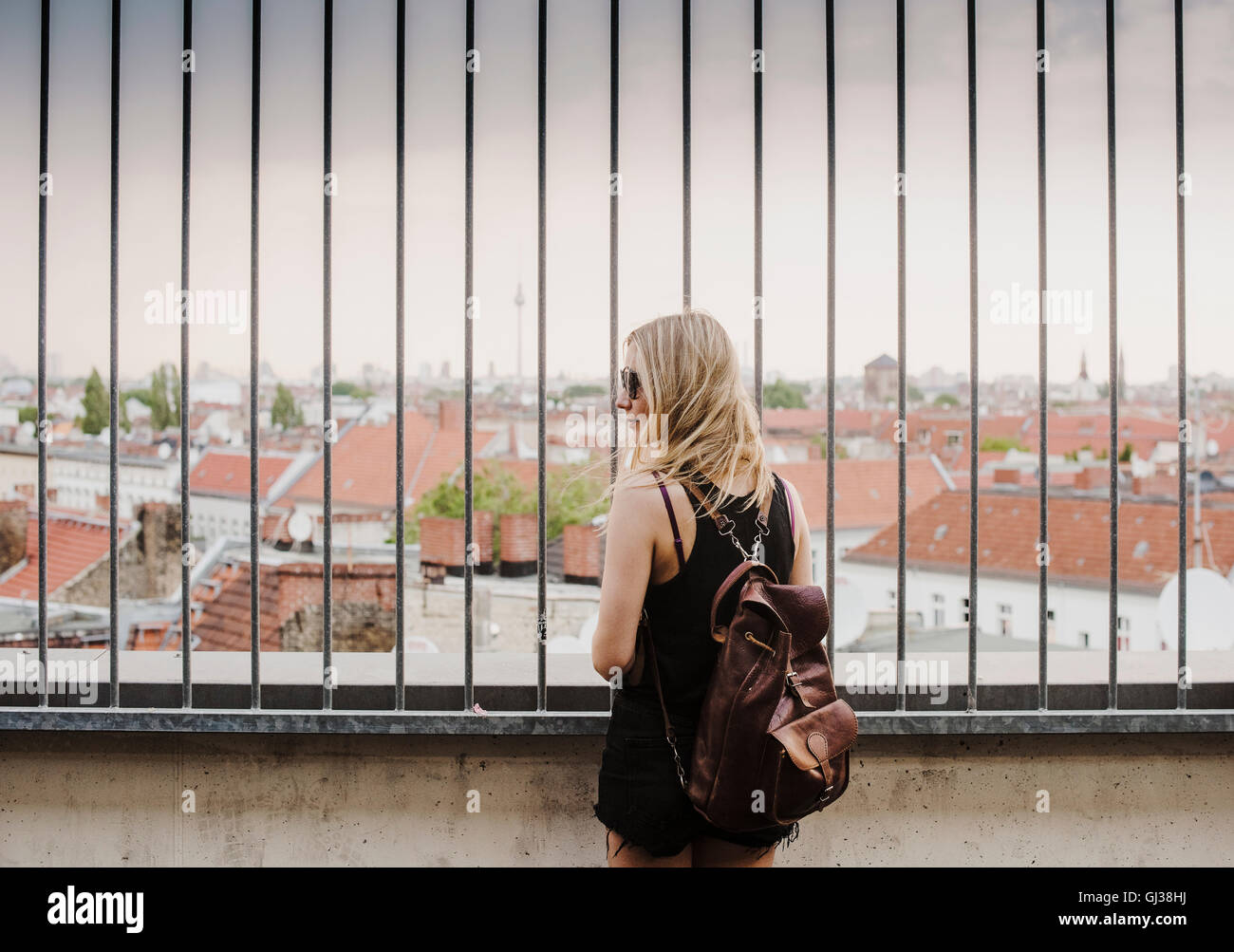 Young woman looking through railings, at view across rooftops, rear ...