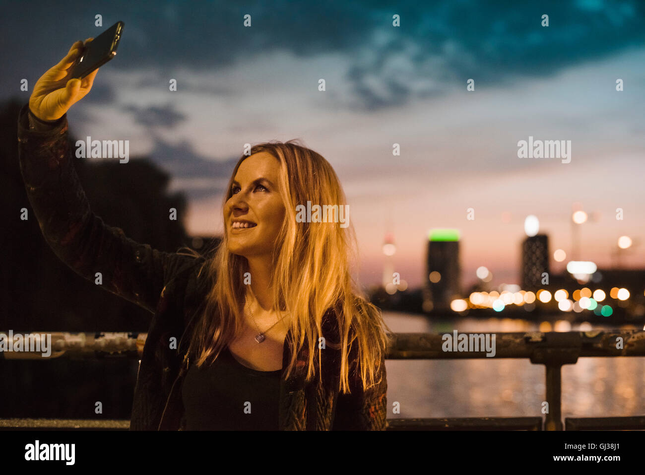 Young woman by waterfront, taking selfie with smartphone Stock Photo ...