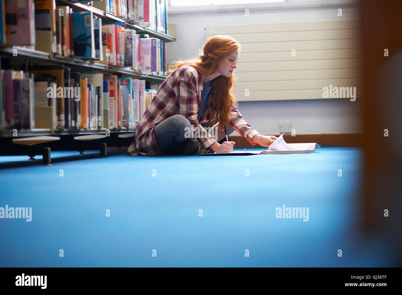 Young female college student writing notes on library floor Stock Photo ...