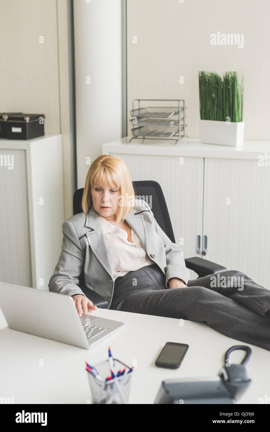 Mature woman with feet on desk hi-res stock photography and images - Alamy