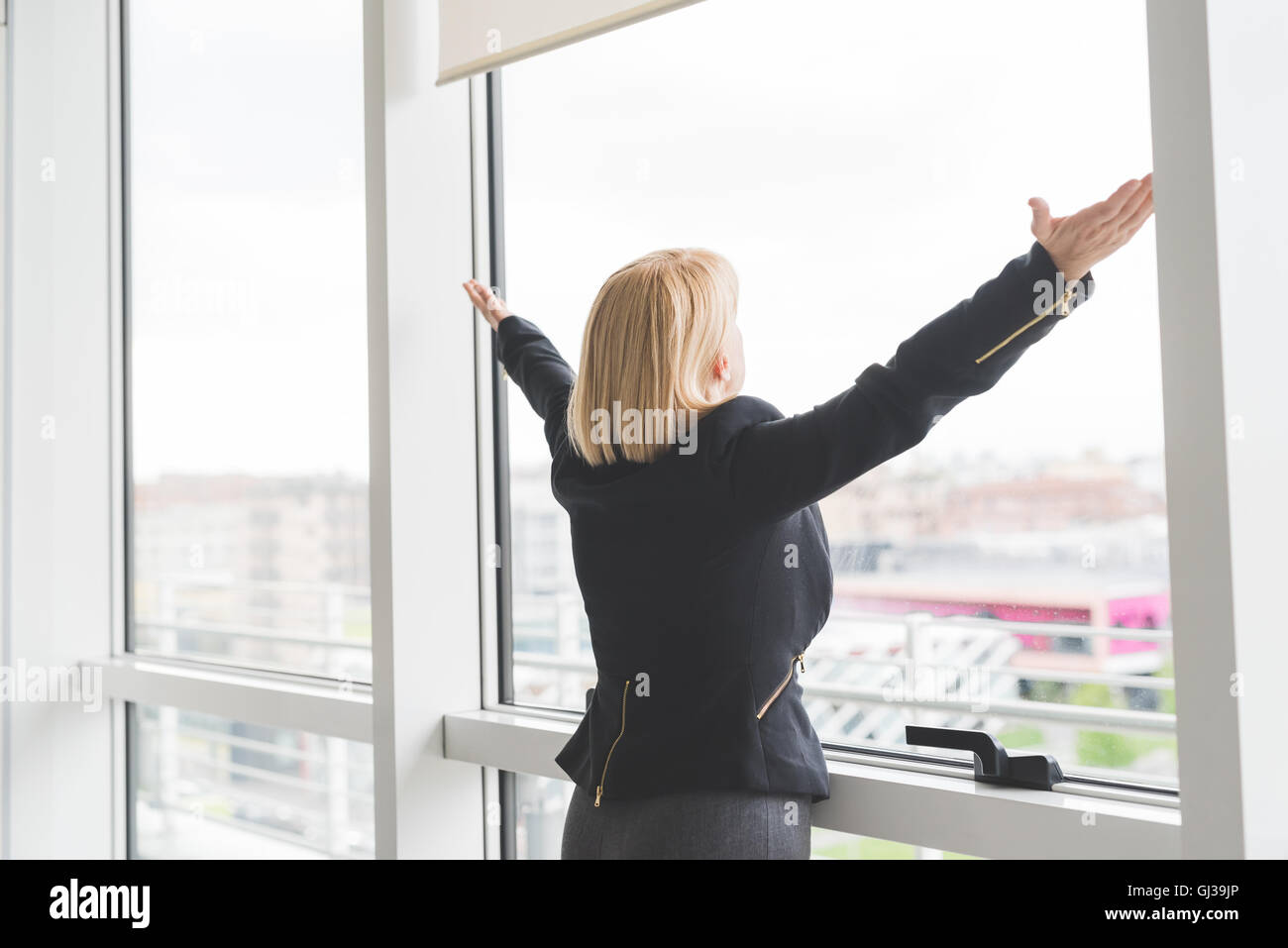 Businesswoman celebrating with open arms at office window Stock Photo ...
