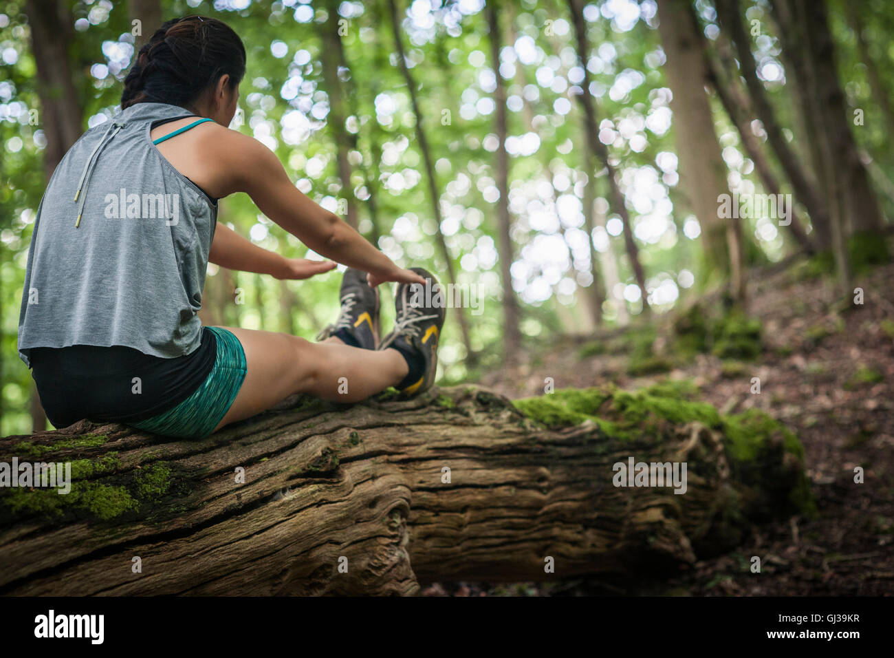 Mid adult woman exercising in forest, sitting on log, stretching Stock ...