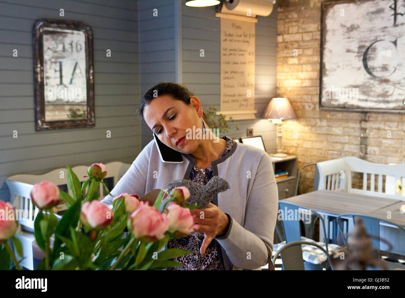 Mature female customer reading menu whilst talking on smartphone in ...