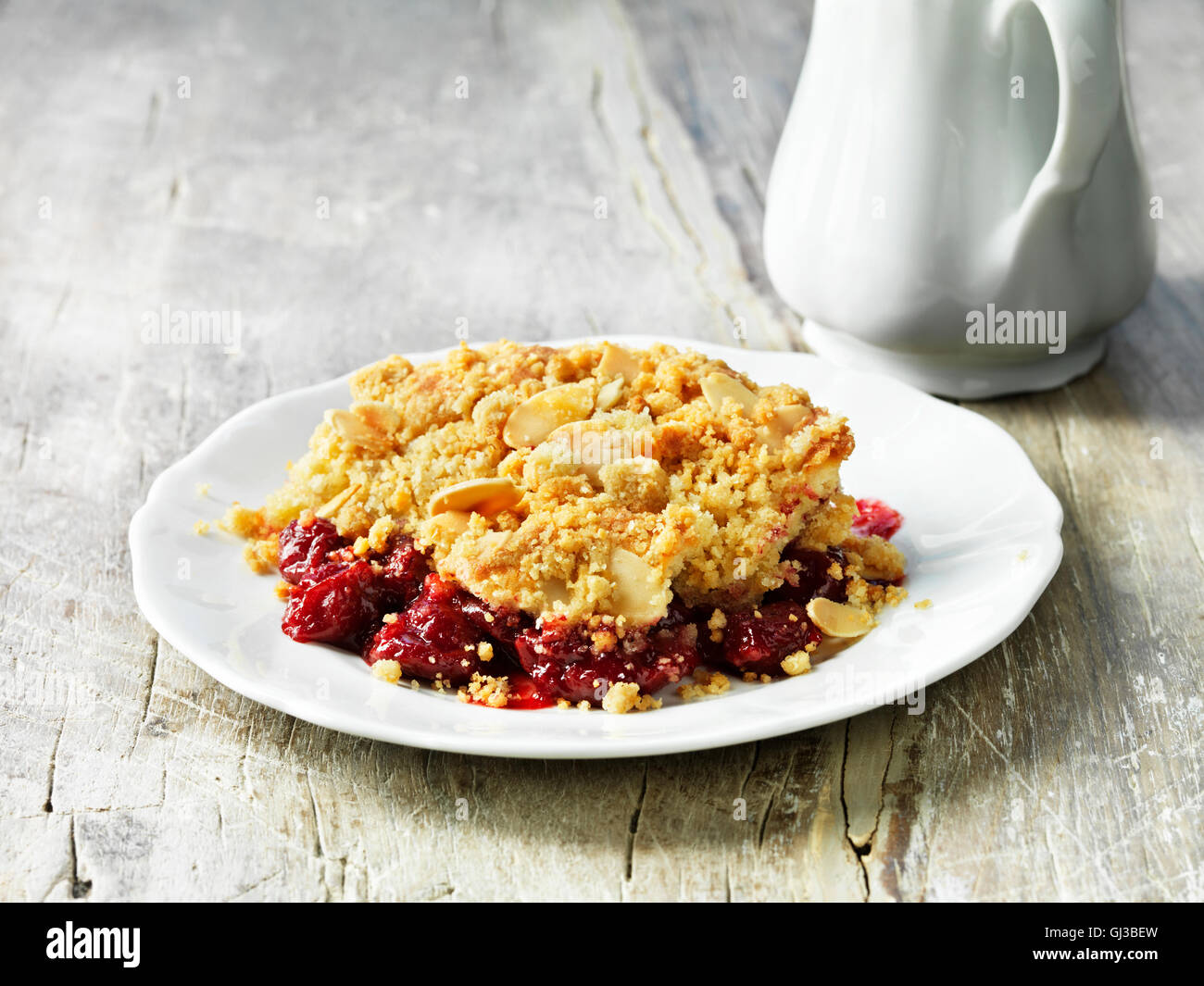 Sour cherry and almond crumble pudding on white plate, white washed ...