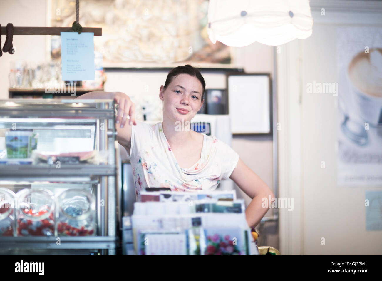 Portrait of young female shop assistant leaning on corner shop counter ...