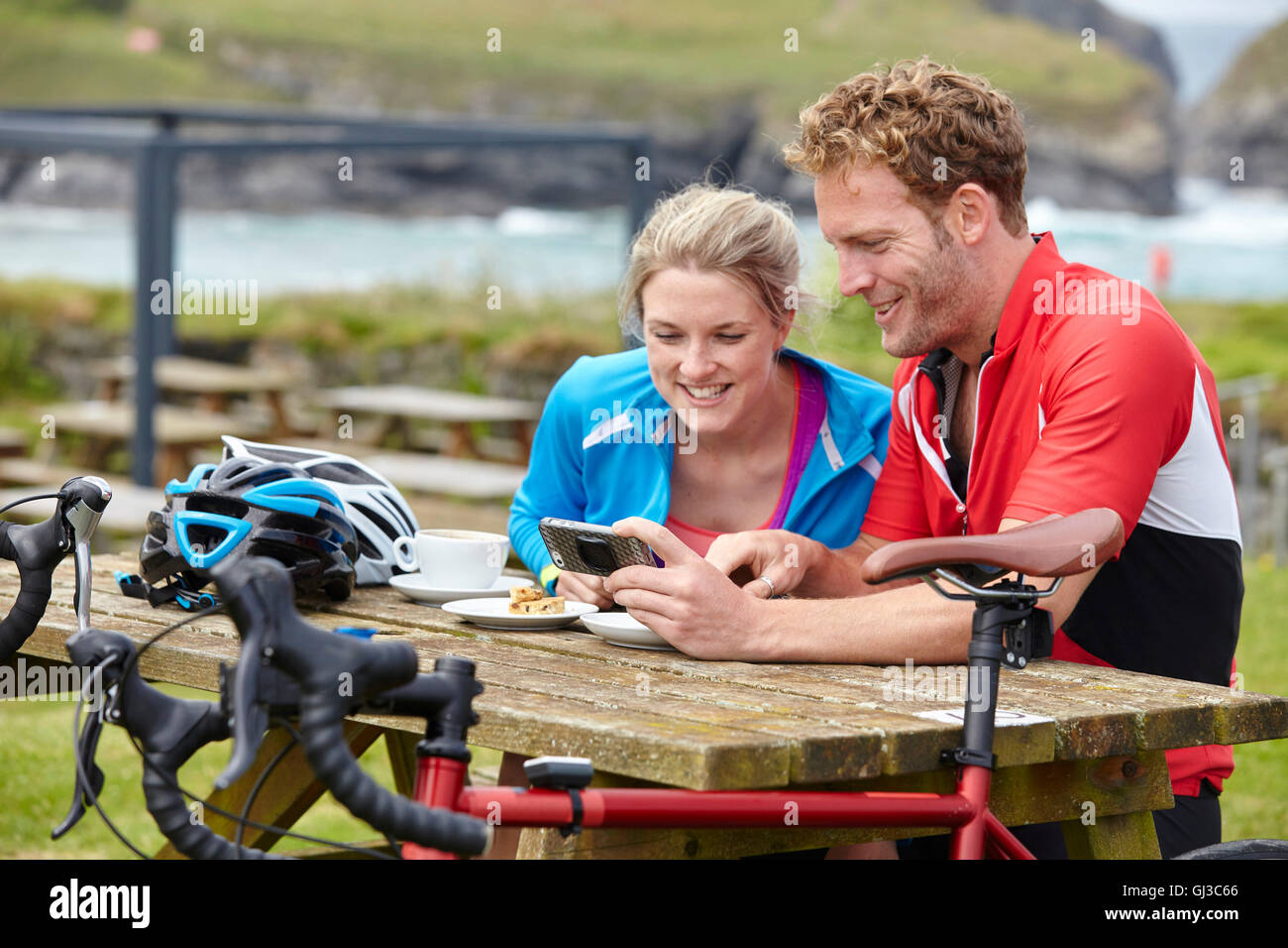 Cyclists using mobile phone at picnic table overlooking ocean Stock ...