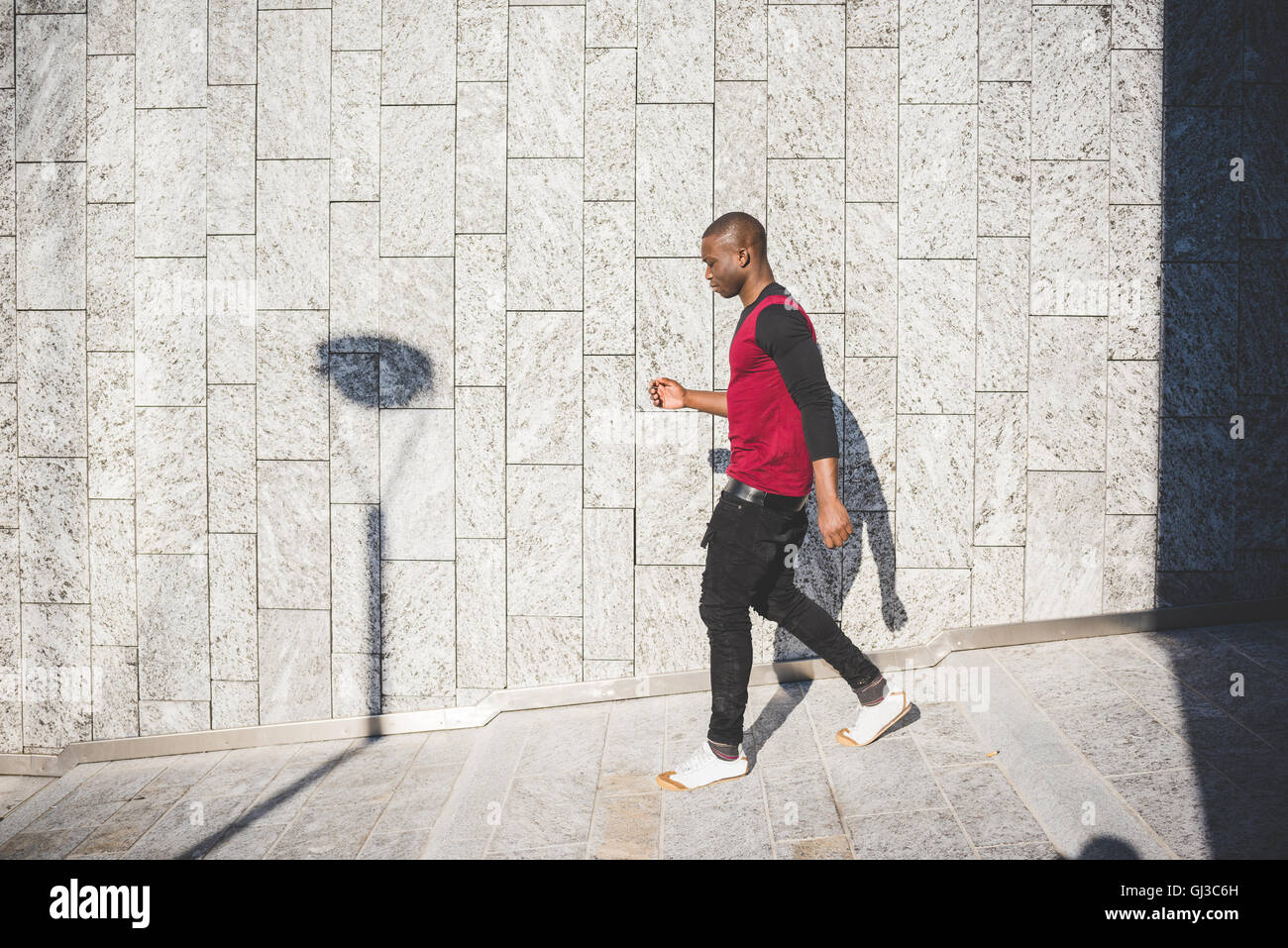 Young man walking outdoors, shadow cast on wall beside him Stock Photo ...