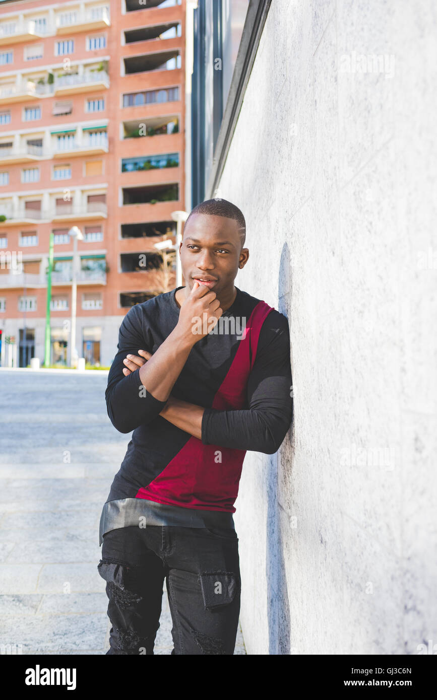 Portrait of young man leaning against wall, hand on chin, thoughtful ...