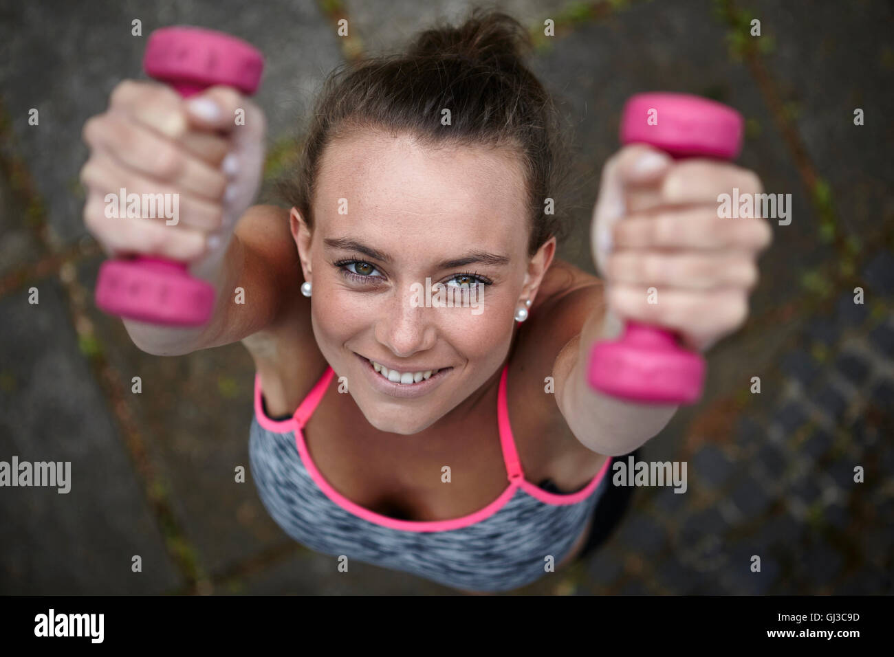 Overhead portrait of young woman training, weight lifting pink ...
