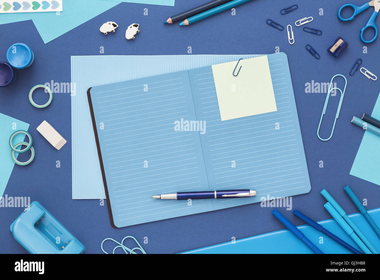 Open notebook and sticky note on blue desk. Scrapbook and supplies on ...