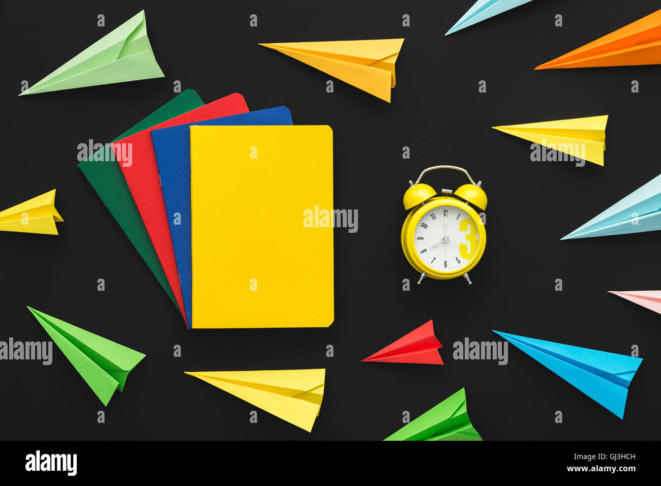 Multicolor notebooks with paper, origami planes and alarm clock on the ...