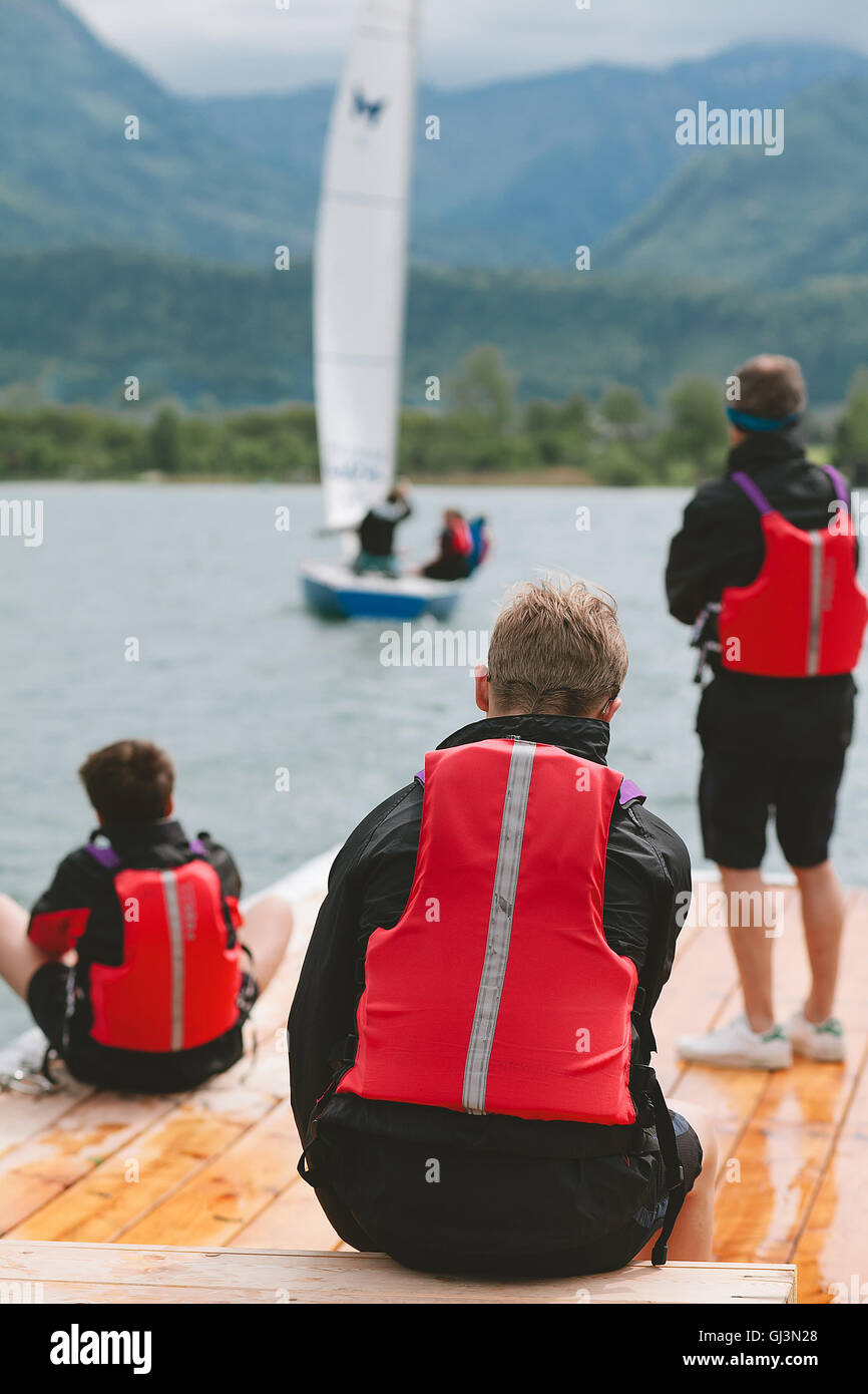 sailing students wearing red buoyancy aids watch whilst their friends ...