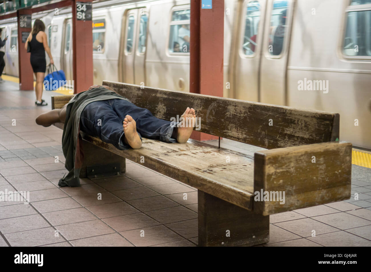 A homeless individual sleeps on a bench in a subway station in New York ...