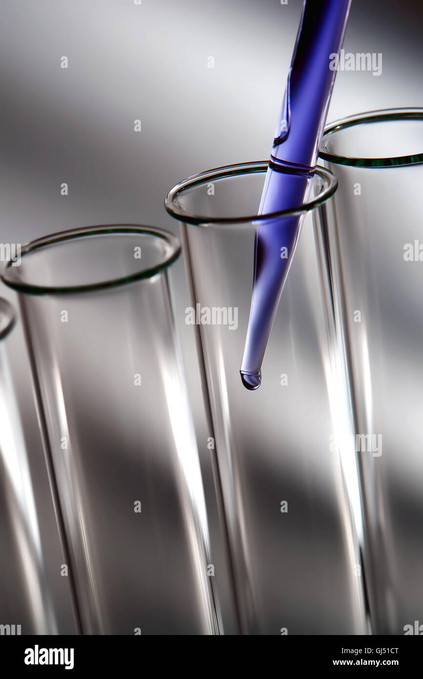 Laboratory pipette with drop of blue liquid over empty glass test tubes ...