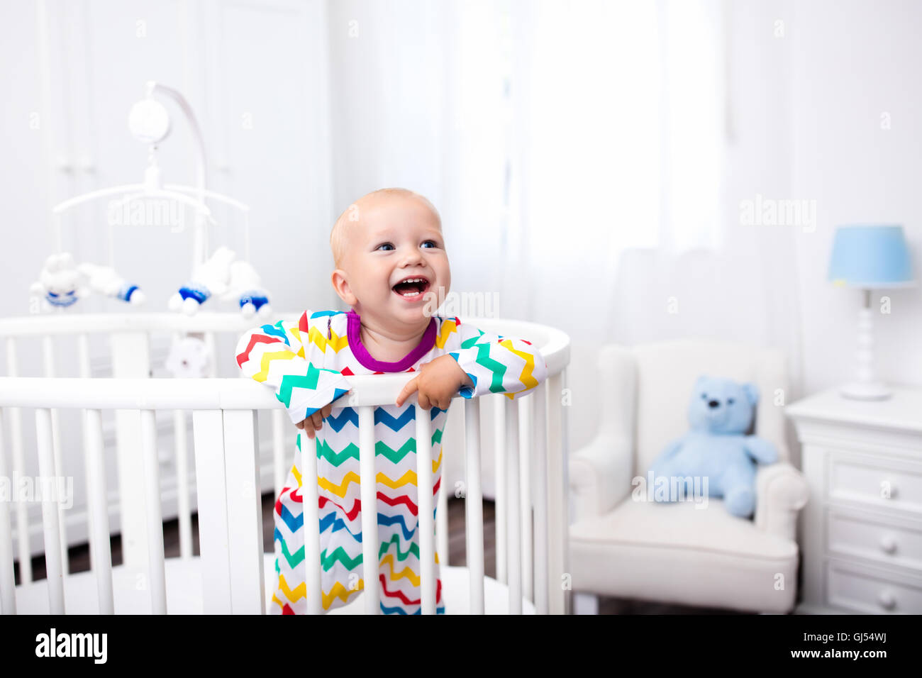 Cute laughing baby standing in bed after nap time. Nursery interior for ...