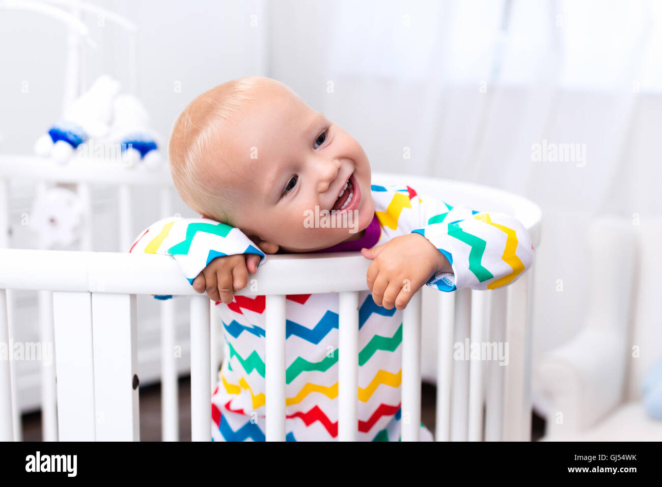 Cute laughing baby standing in bed after nap time. Nursery interior for ...