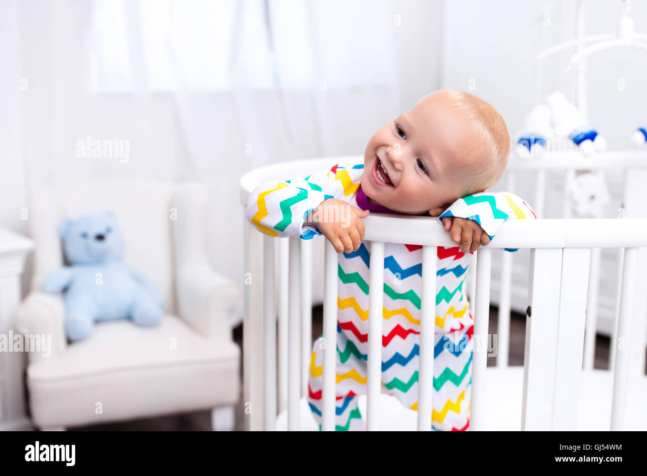 Cute laughing baby standing in bed after nap time. Nursery interior for ...