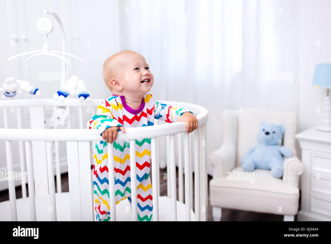 Cute laughing baby standing in bed after nap time. Nursery interior for ...