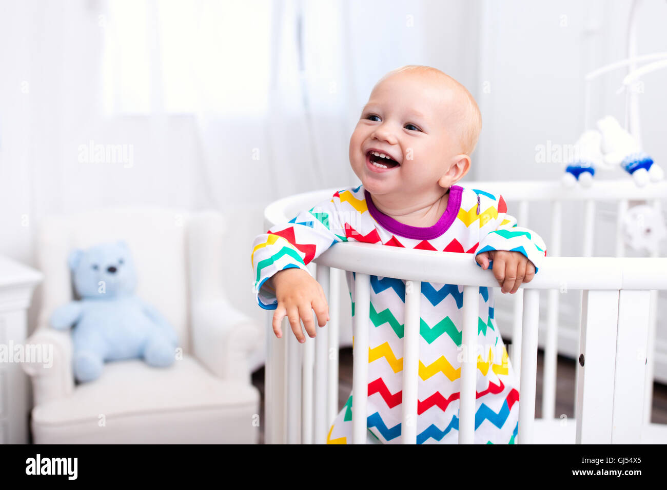 Cute laughing baby standing in bed after nap time. Nursery interior for ...