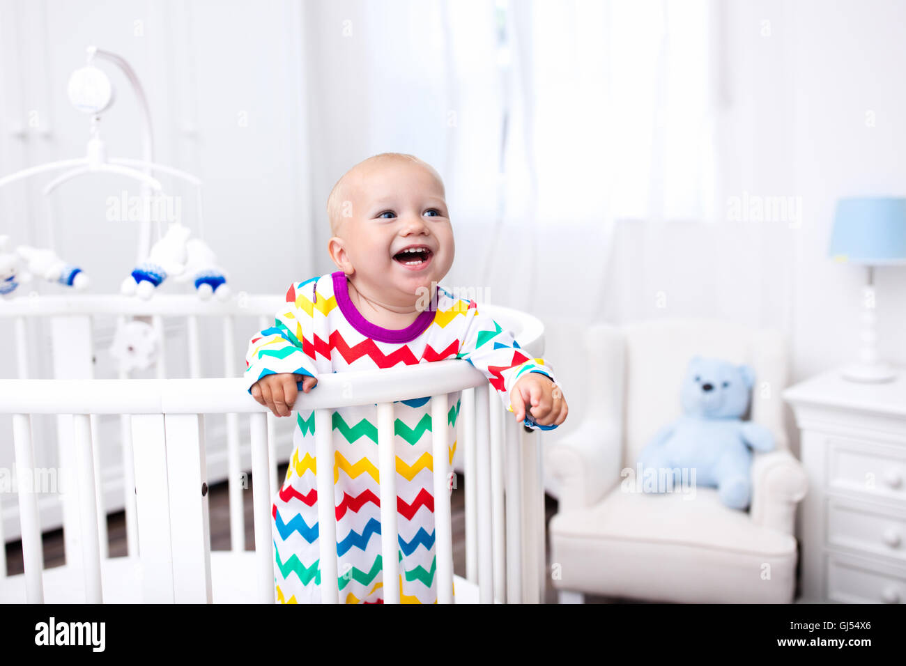 Cute laughing baby standing in bed after nap time. Nursery interior for ...