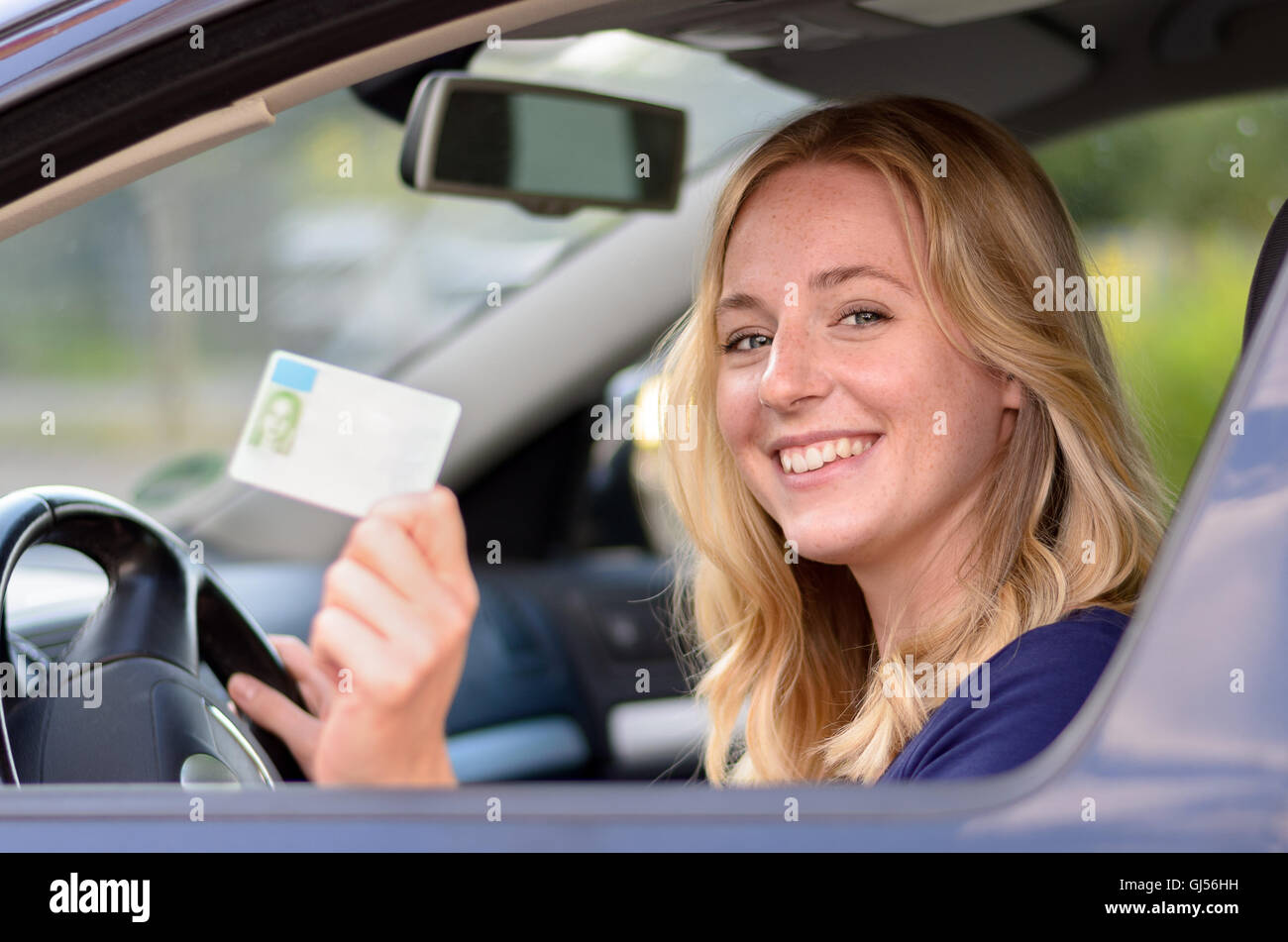 Happy young blond woman sitting behind the steering wheel of a car ...