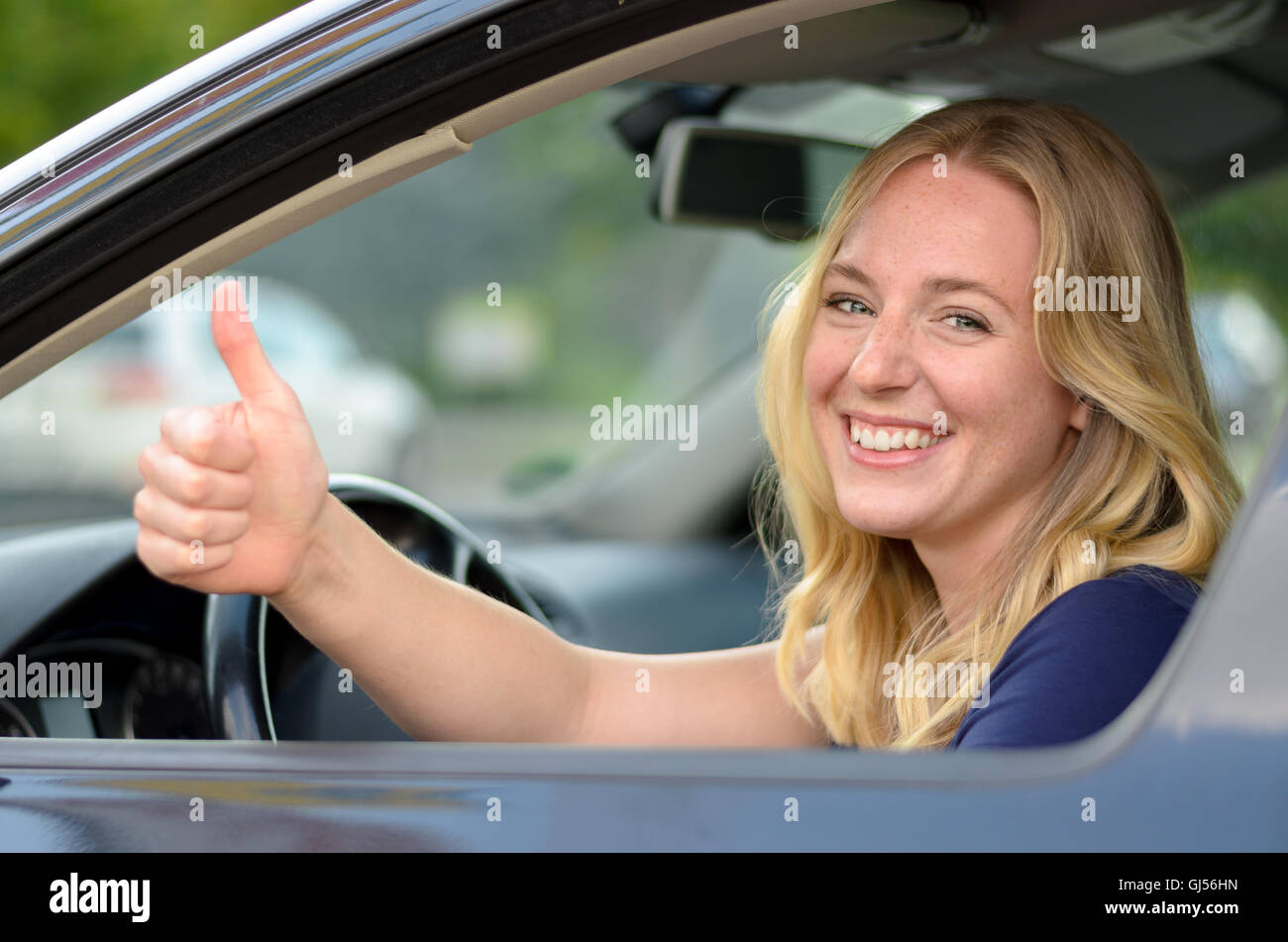 Pretty young blond female driver giving a thumbs up of success and ...