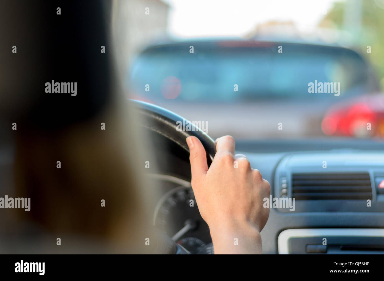 Young woman driving in traffic viewed from behind over hear shoulder ...