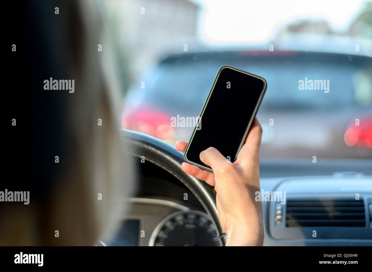 Young woman driver reading a text message on her mobile while driving ...