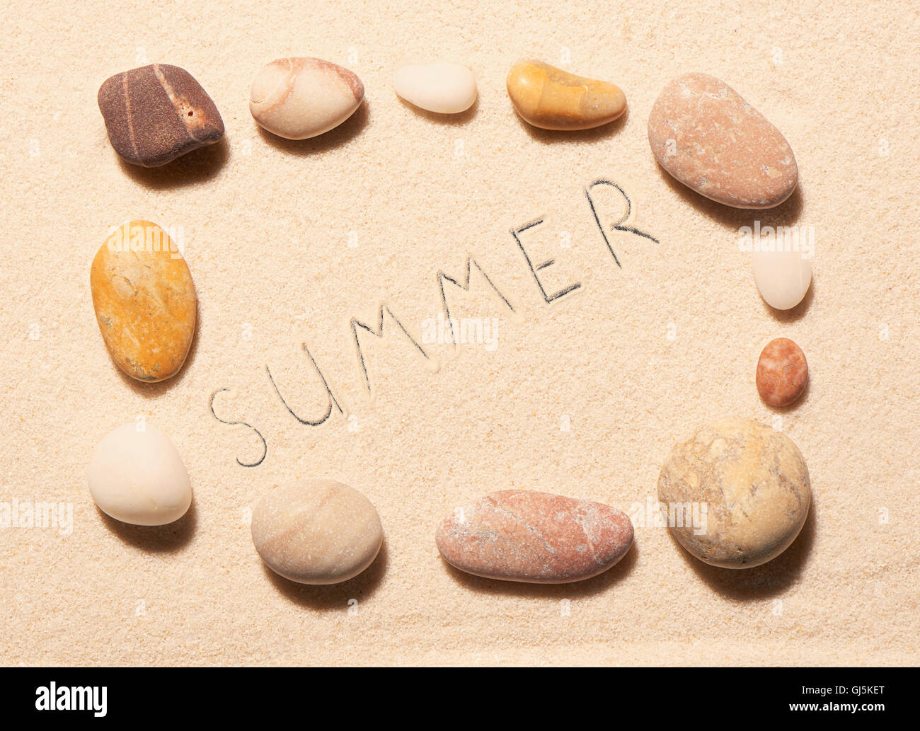 Rectangular frame of sea stones with summer lettering drawn on sand ...