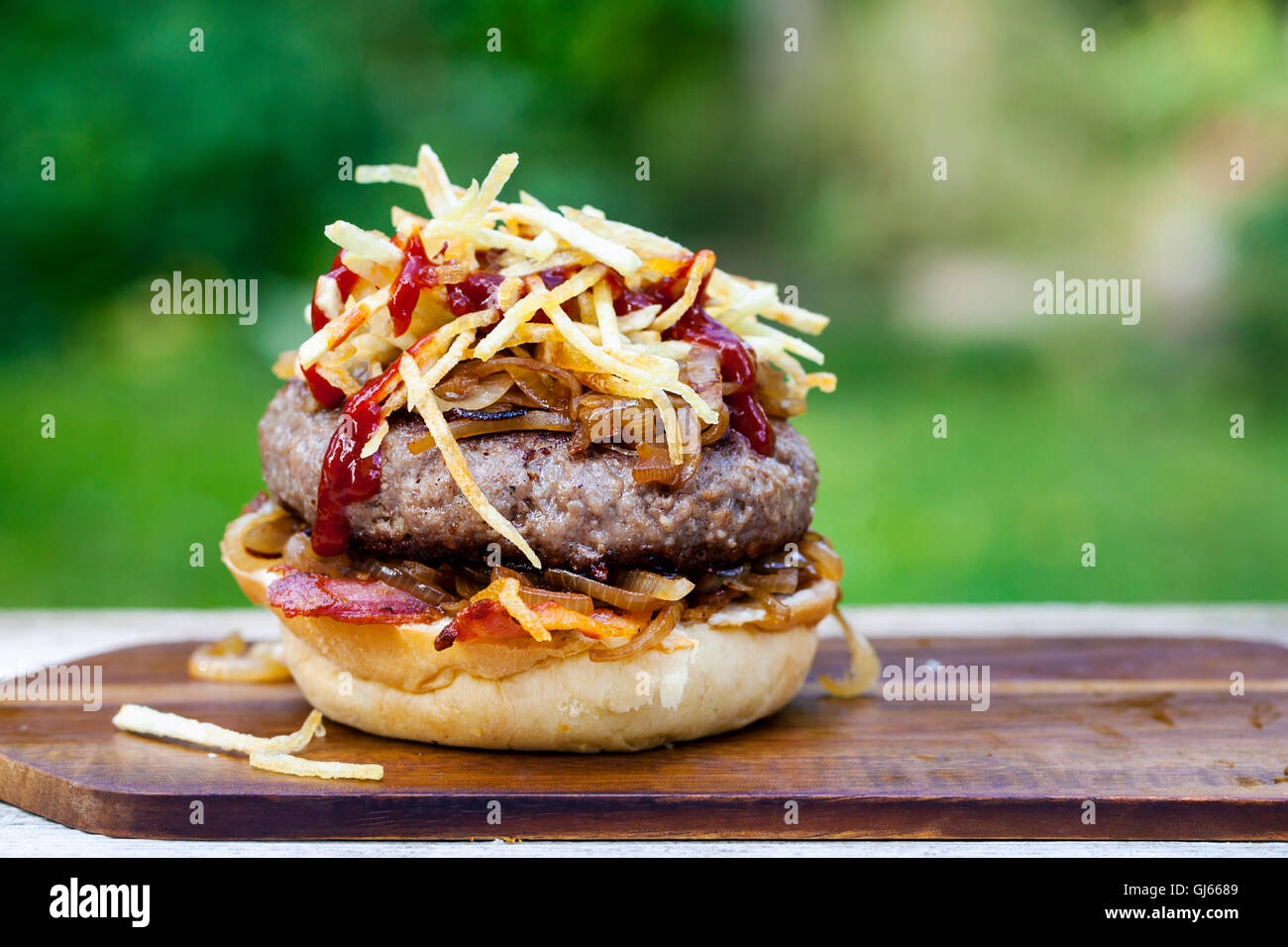 Beefburger with fried onions, bacon and string fries in brioche bun ...
