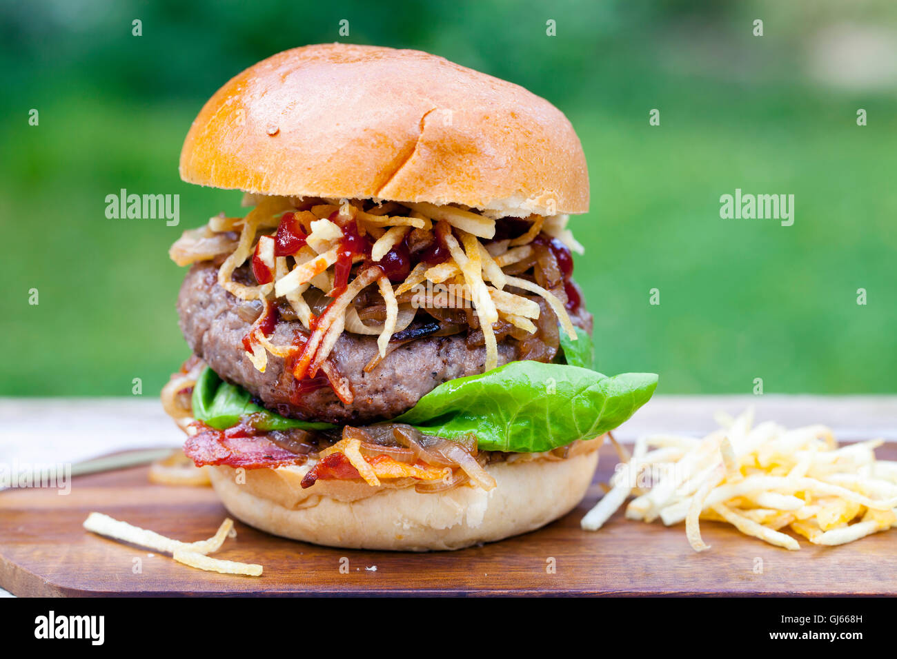 Beefburger with fried onions, bacon and string fries in brioche bun ...