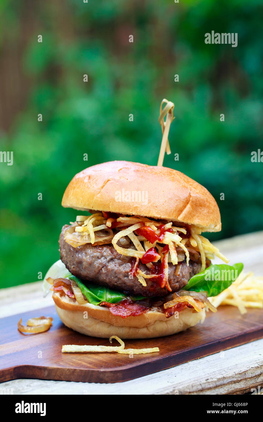Beefburger with fried onions, bacon and string fries in brioche bun ...