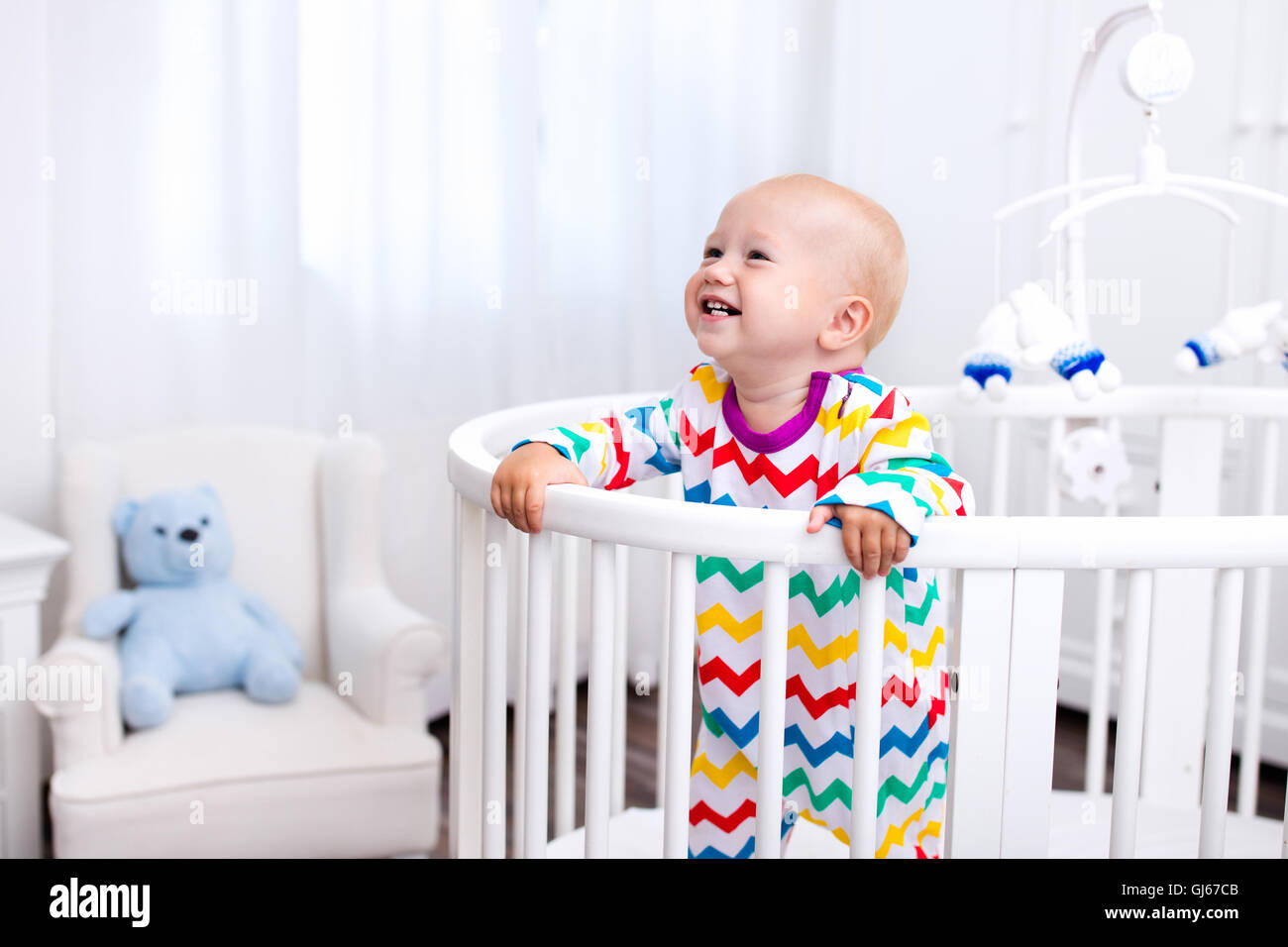 Cute laughing baby standing in bed after nap time. Nursery interior for ...