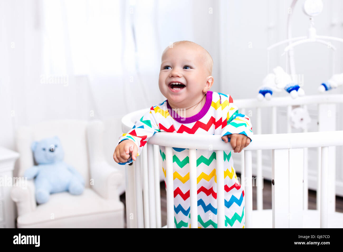 Cute laughing baby standing in bed after nap time. Nursery interior for ...
