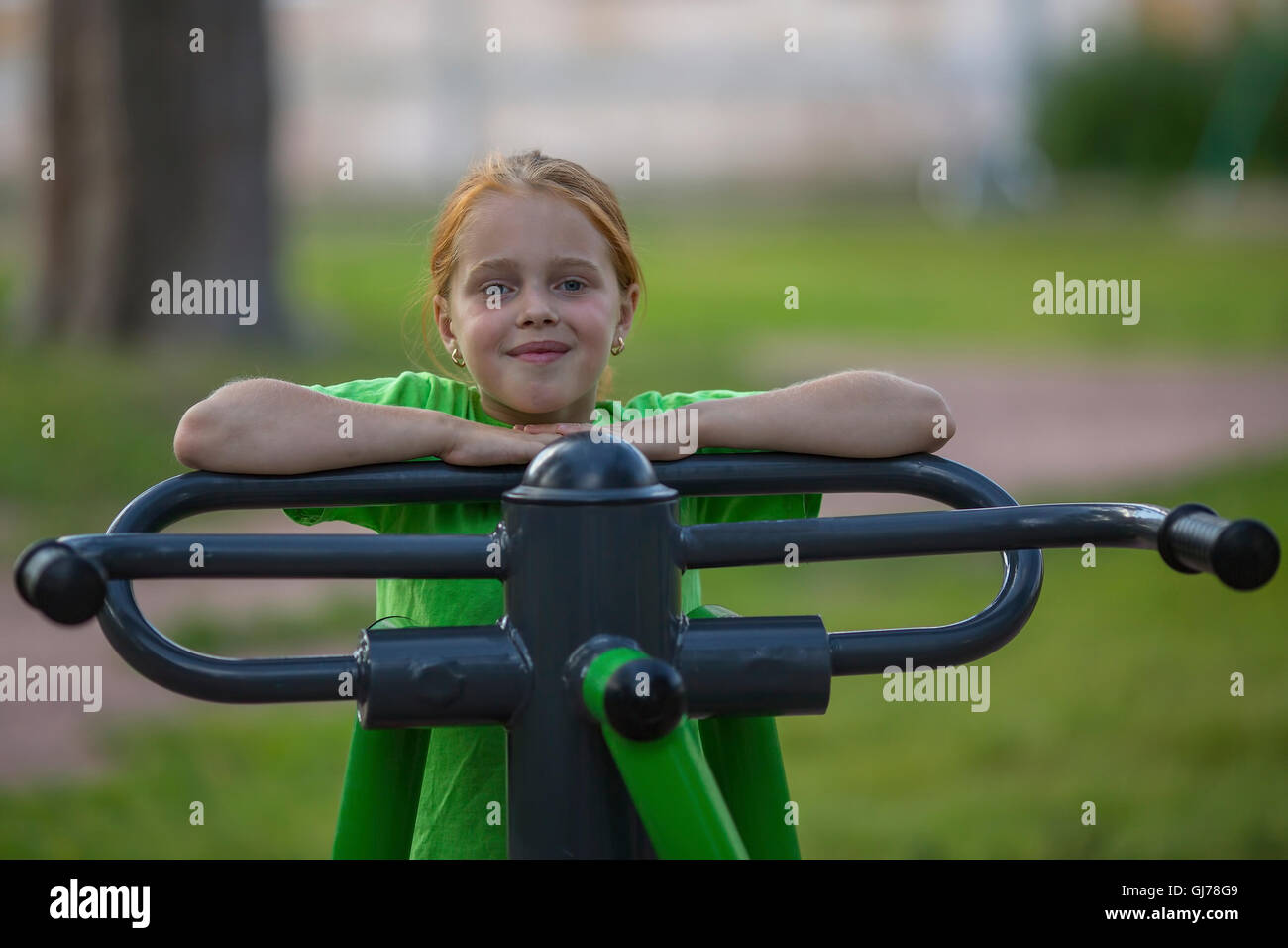 Portrait of little girl sitting on exercise equipment in the public ...