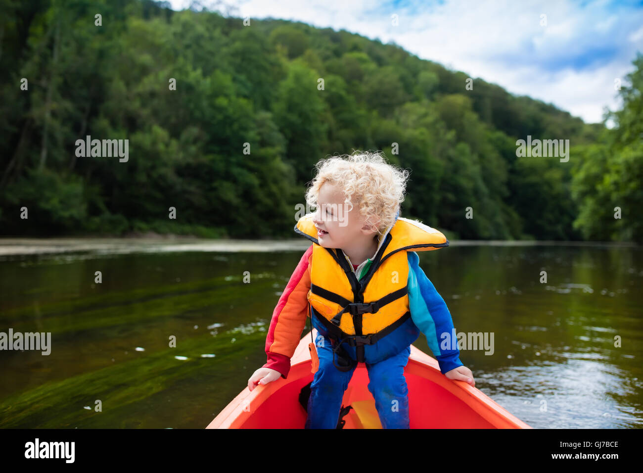 Happy kid enjoying kayak ride on beautiful river. Little curly toddler ...