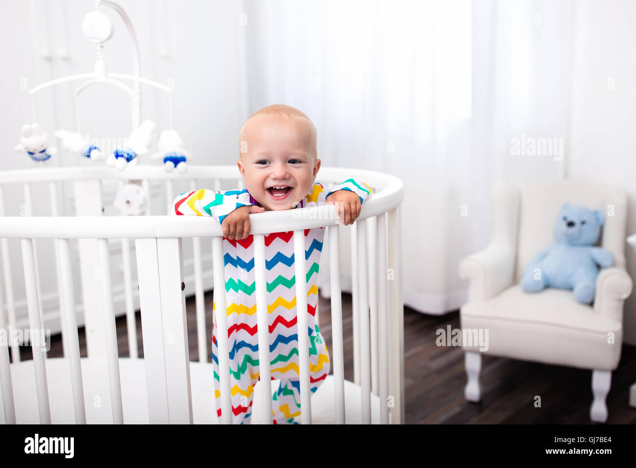 Cute laughing baby standing in bed after nap time. Nursery interior for ...