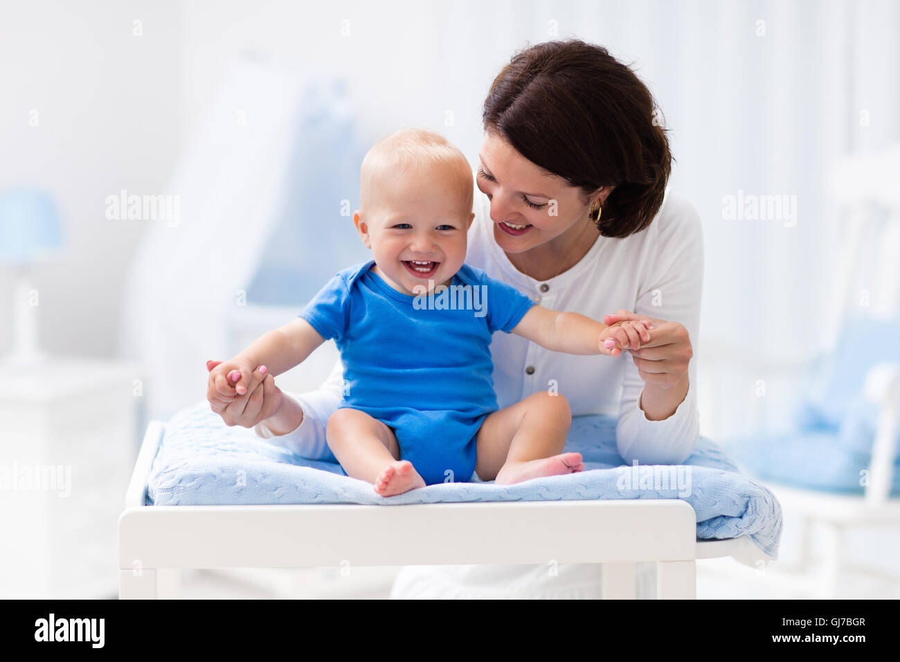 Young mother taking care of little boy in white sunny nursery with ...