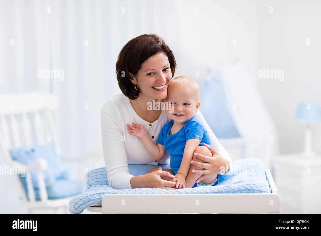 Young mother taking care of little boy in white sunny nursery with ...