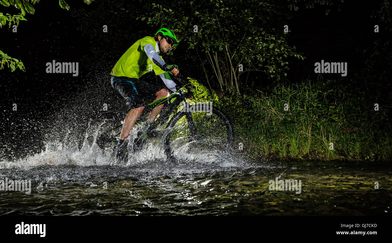 Mountain biker riding in forest stream, splashing water around Stock ...