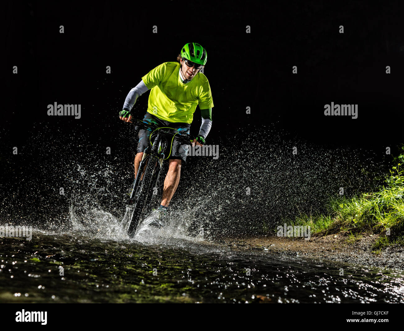 Mountain biker riding in forest stream, splashing water around Stock ...