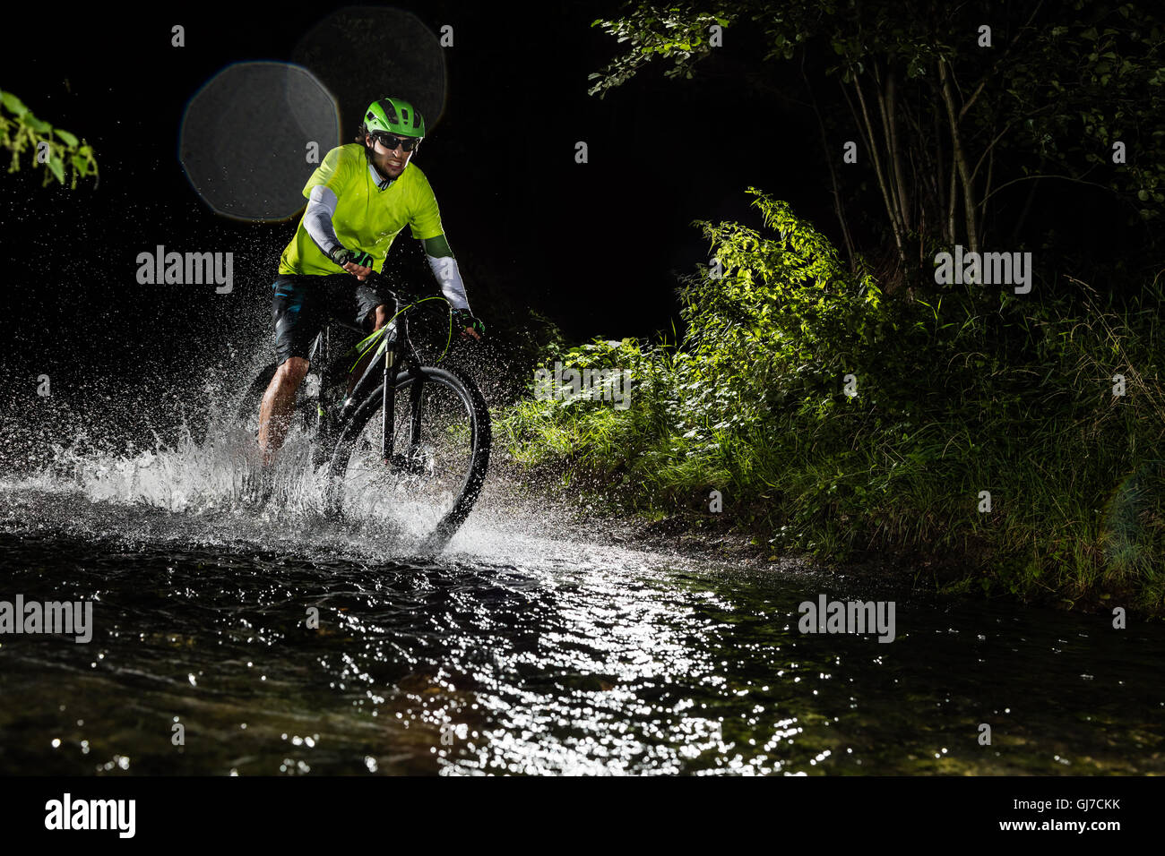 Mountain biker riding in forest stream, splashing water around Stock ...