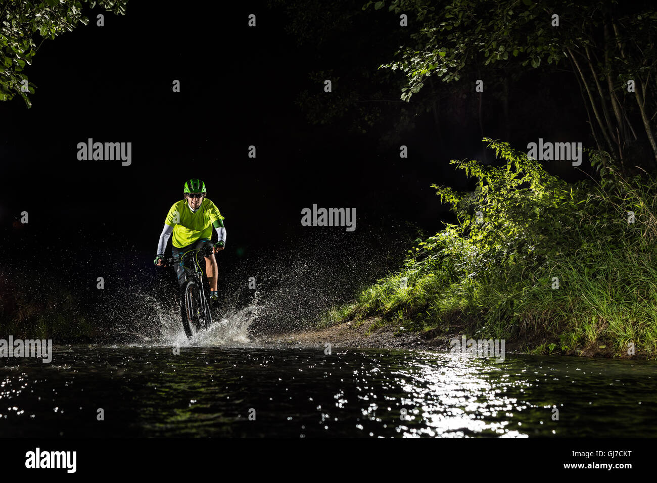 Mountain biker riding in forest stream, splashing water around Stock ...